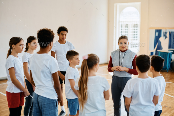 Young sports teacher talking to group of school kids during PE class ...