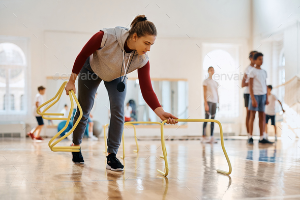 Female sports teacher setting obstacles during physical education class ...