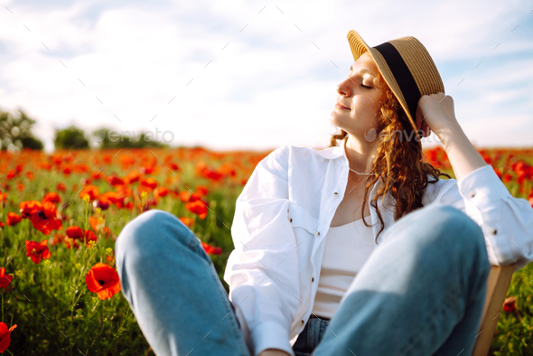Young curly girl posing in a poppy field sitting on a chair. Summertime ...