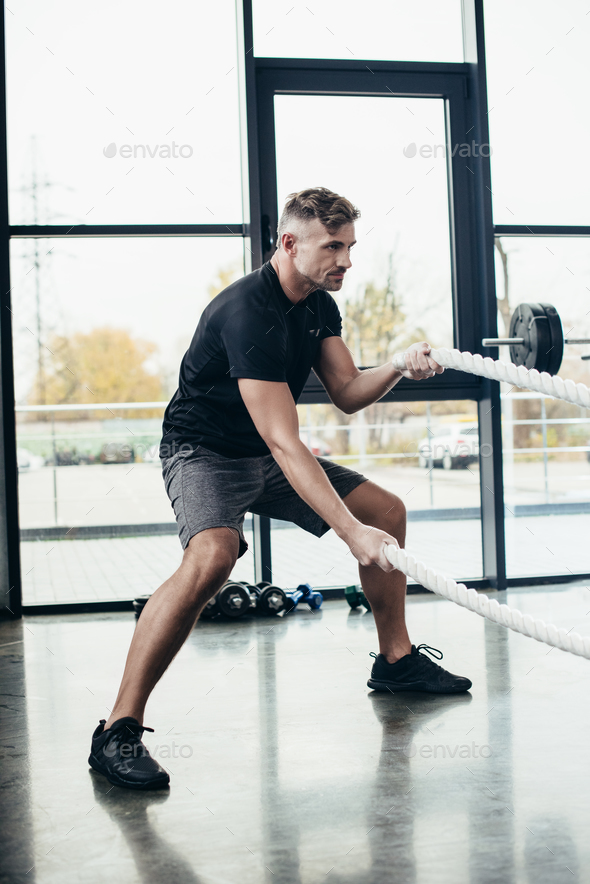 side view of handsome sportsman working out with ropes in gym Stock ...