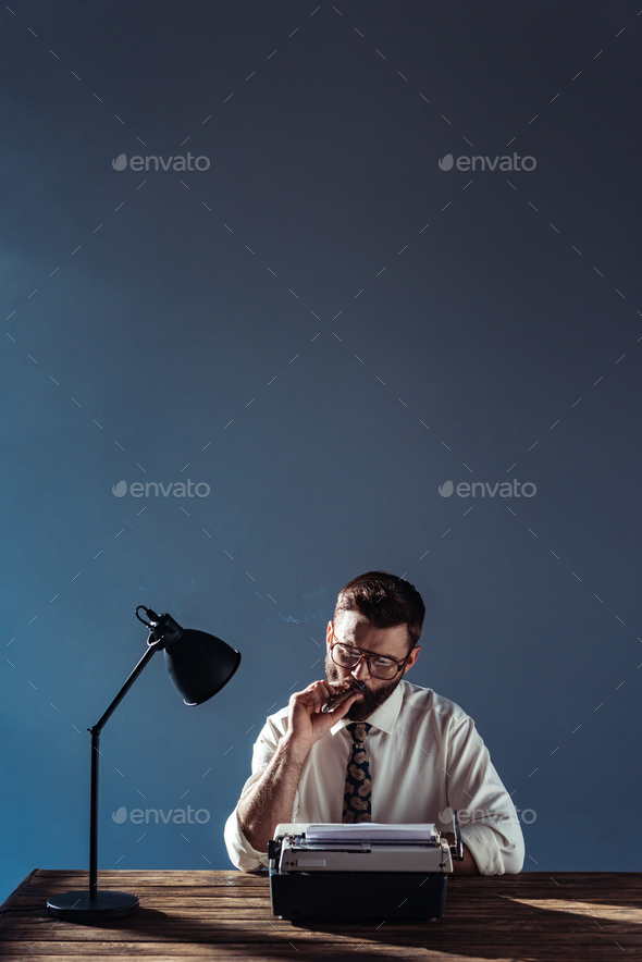 handsome journalist sitting at table with lamp and retro typewriter and ...