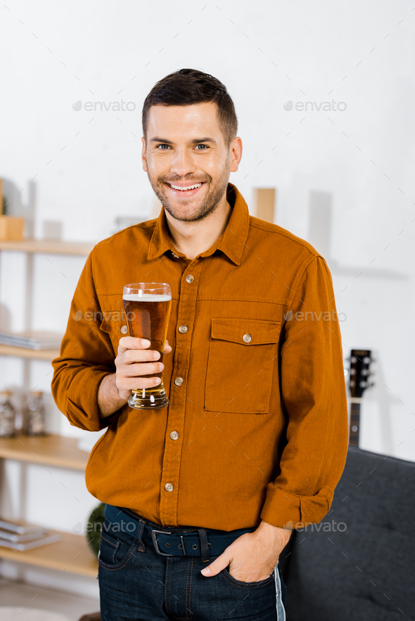handsome man in modern living room holding glass of beer and putting ...