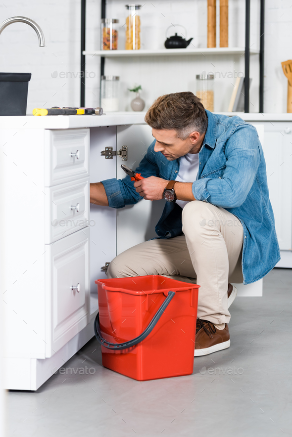 handsome adult man repairing kitchen sink Stock Photo by LightFieldStudios