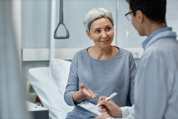 Doctor asking questions to patient in ward Stock Photo by seventyfourimages