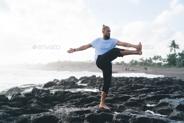 Pumped up male yogi recreating doing balance yoga poses feeling inner ...