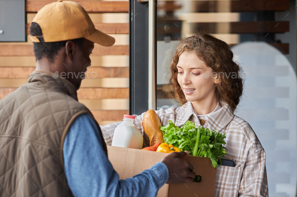 Woman receiving grocery delivery outdoors and holding bag with fresh ...