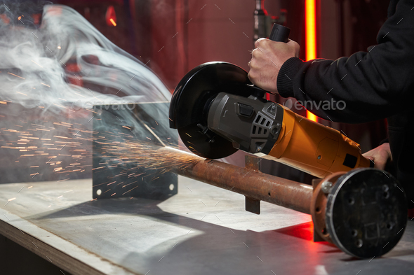 hands holding a powerful angle grinder and sawing a metal pipe on a ...
