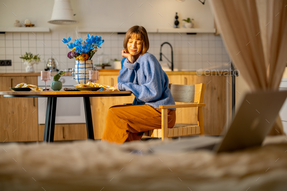 Woman sitting relaxed by the dining table at home Stock Photo by RossHelen