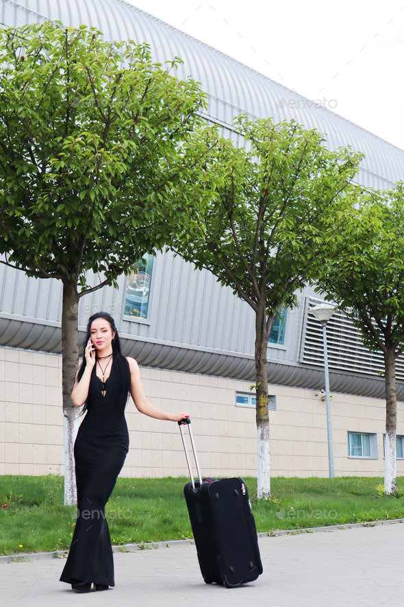 Smiling female passenger proceeding to exit gate pulling suitcase ...