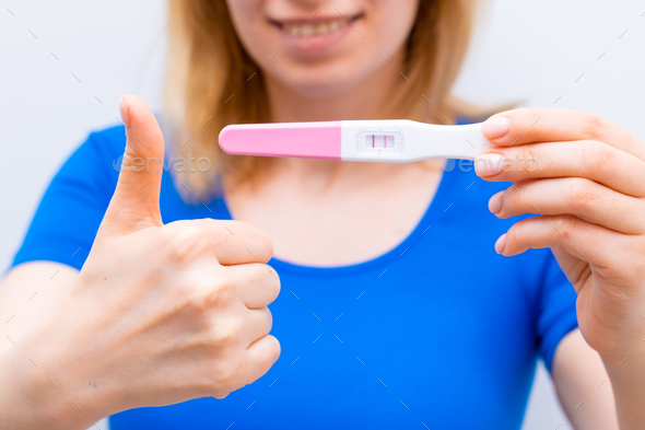 Smiling woman shows sign like and holding a positive pregnancy test ...