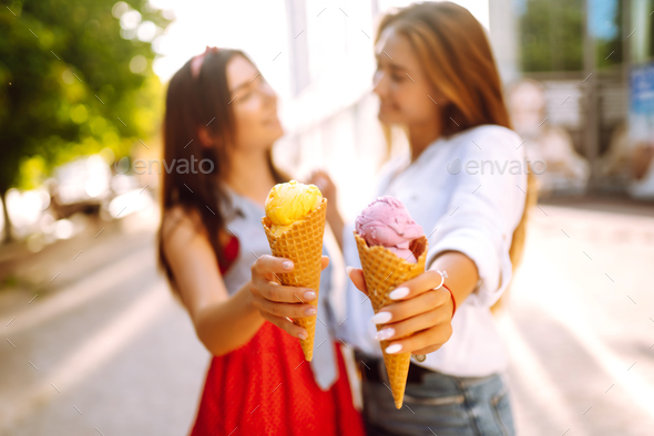 Ice cream in hands of beautiful young girls. Two female friends eat ice ...