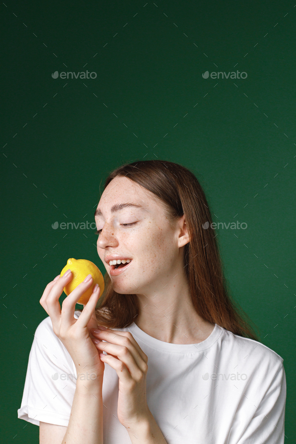 Studio portrait of a girl model holding a lemon isolated on green ...