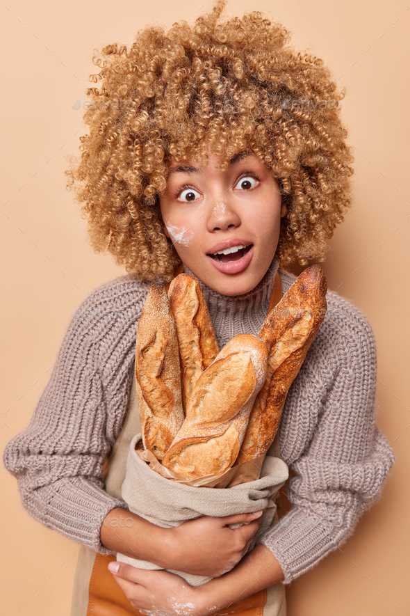 Impressed curly haired female baker holds crusty delicious baked ...