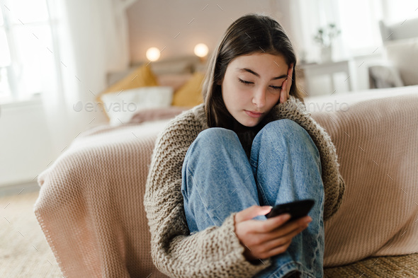 Teenage girl sitting on the floor and scrolling her smartphone. Stock Photo by halfpoint