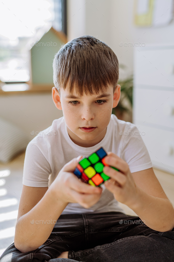 Little boy playing with Rubiks cube in his room. Stock Photo by halfpoint