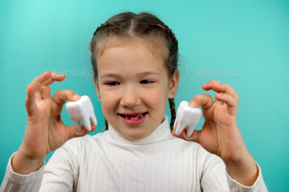Beautiful little happy Caucasian girl holding little model of tooth on ...