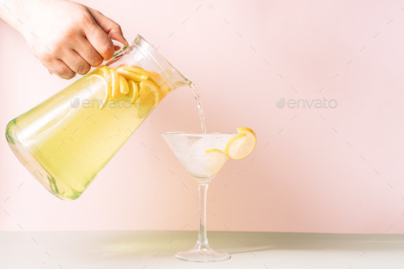 Man's hand pouring lemonade into glass goblet with lime against pink ...