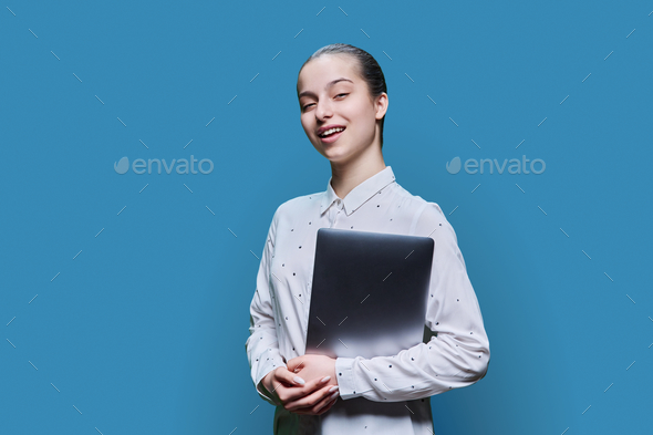 Teenage girl holding closed laptop in her hands, on blue studio ...