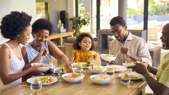 Multi-Generation Family Sitting Around Table Serving Food For Meal At ...