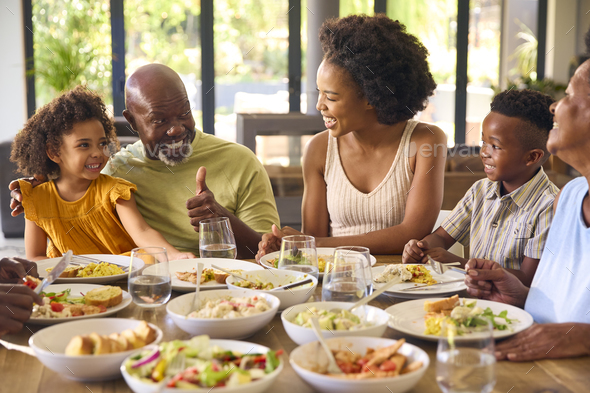 Multi-Generation Family Sitting Around Table Eating Meal At Home ...