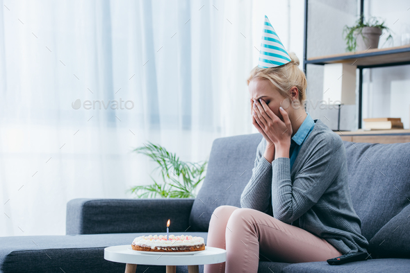 upset woman in party hat crying while celebrating birthday at home ...