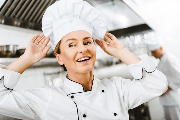 beautiful smiling female chef adjusting cap in restaurant kitchen Stock ...