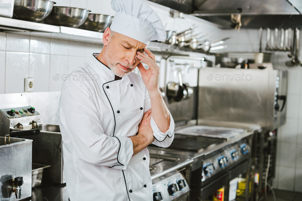 tired male chef in uniform touching head and having headache in ...