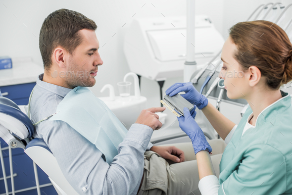 handsome patient pointing with finger at teeth color palette near ...