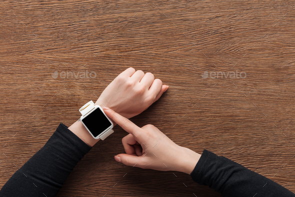 Cropped view of girl using smartwatch with blank screen on wooden ...