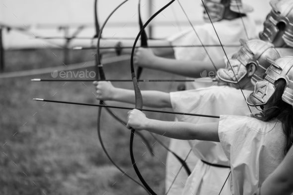 Grayscale shot of a group of people firing arrows with bows at a target ...