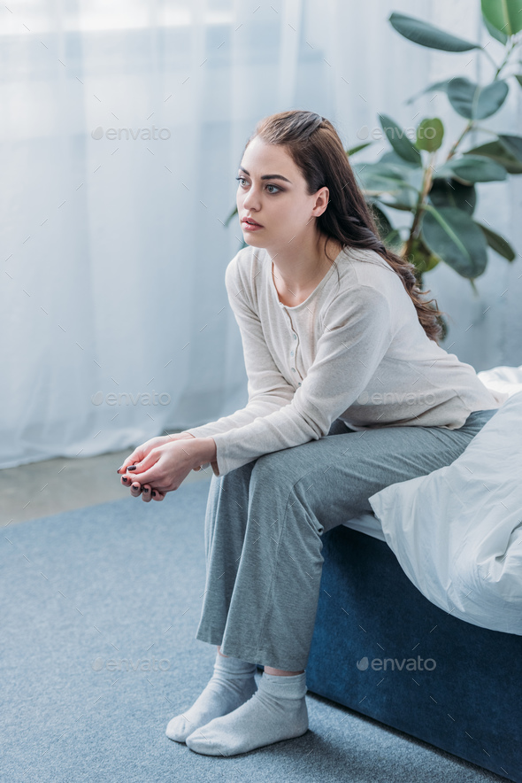 sad woman in pajamas with folded hands sitting on bed at home Stock ...