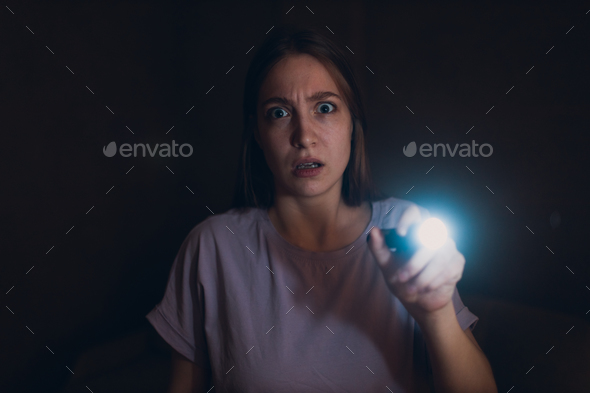 Woman scared holding hand flashlight in darkness and afraid of violence ...