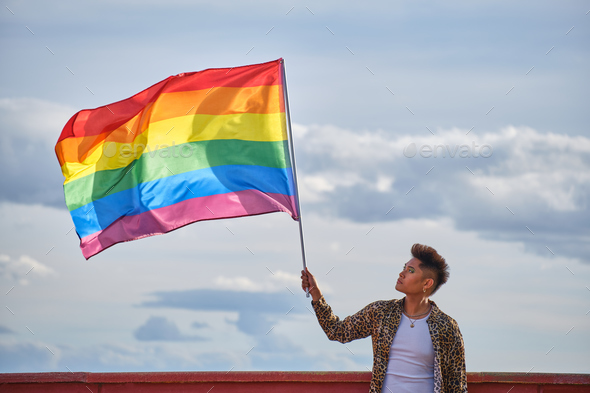 gender non binary asian person holding rainbow gay pride flag on sky ...