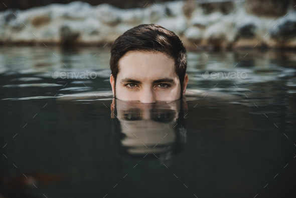 A horizontal shot of a man in a water pond with half of his face ...