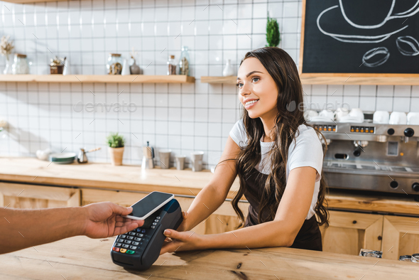 attractive cashier standing near bar counter in brown apron and holding ...