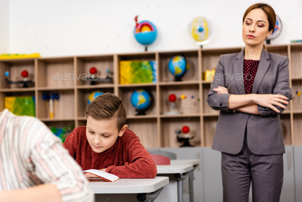 Serious teacher in suit standing with crossed arms and looking at ...