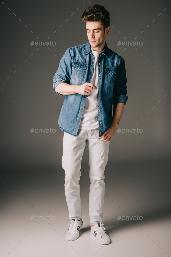 handsome man in denim shirt and jeans looking away on grey background ...