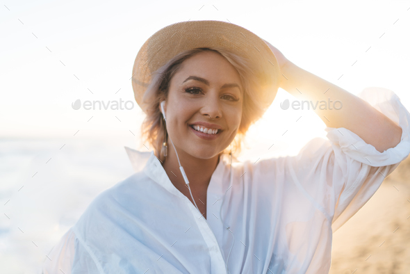 Happy millennial tourist in stylish hat using electronic headphones for ...