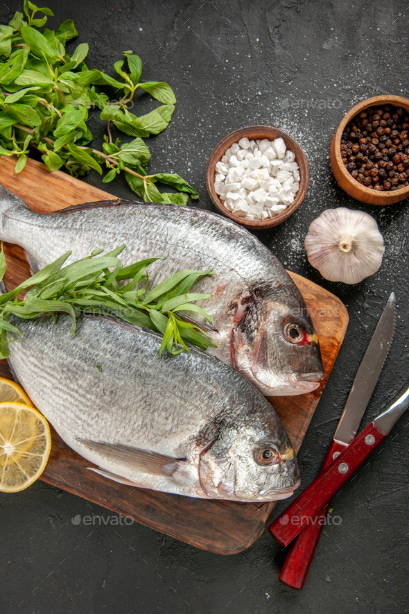 top view raw sea fish on chopping board sea salt black pepper in bowls ...