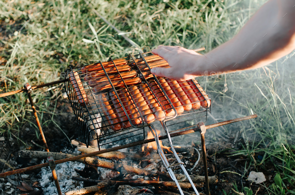 Picnic in nature in summer. Man's hand checking heat from fire while ...
