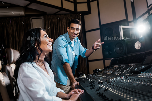 smiling handsome sound producer pointing with finger near pretty ...