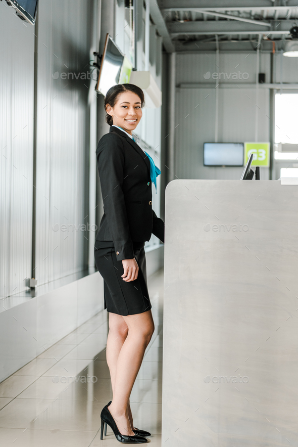 smiling african american airport staff in uniform standing at check in ...