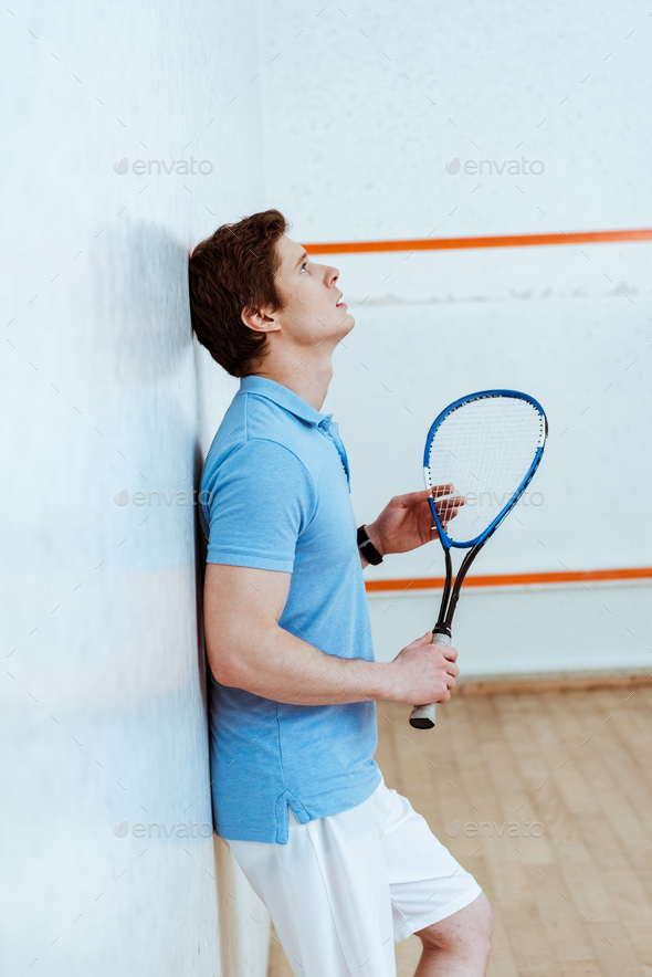 Side view of sad squash player holding racket in four-walled court ...
