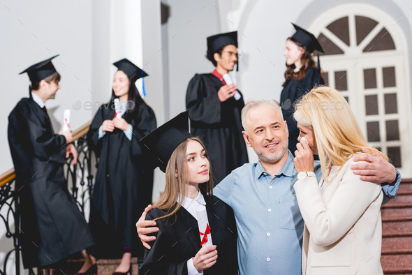 selective focus of attractive girl in graduation cap looking at crying ...