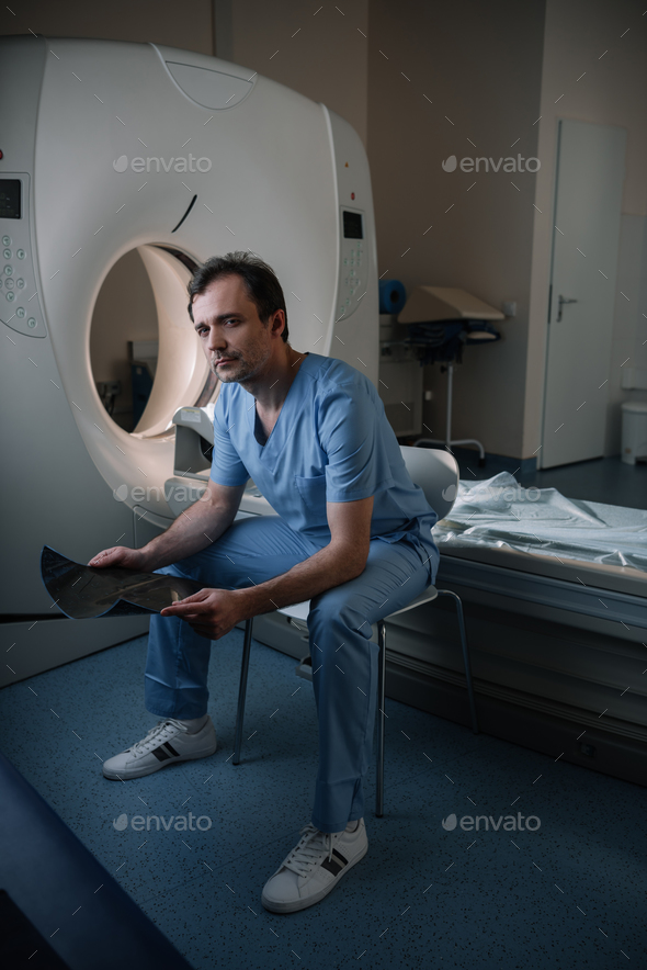 serious radiologist holding x-ray diagnosis while sitting near computed ...
