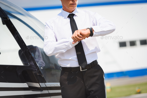 cropped view of Pilot in formal wear adjusting watch near helicopter ...