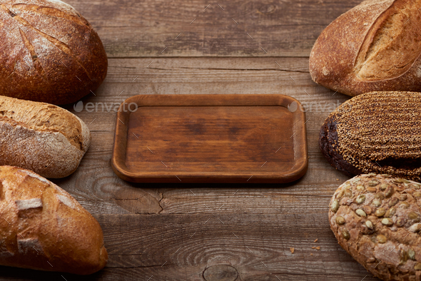 delicious loaves of bread around empty board on wooden table Stock ...