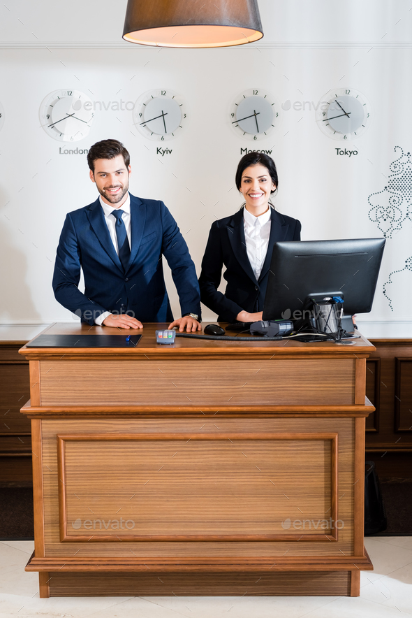 cheerful receptionists in formal wear standing at reception desk Stock ...