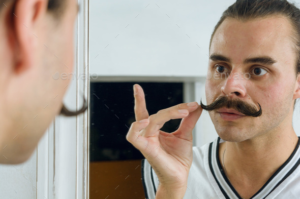 non-binary gender person in front of the mirror fixing his mustache ...