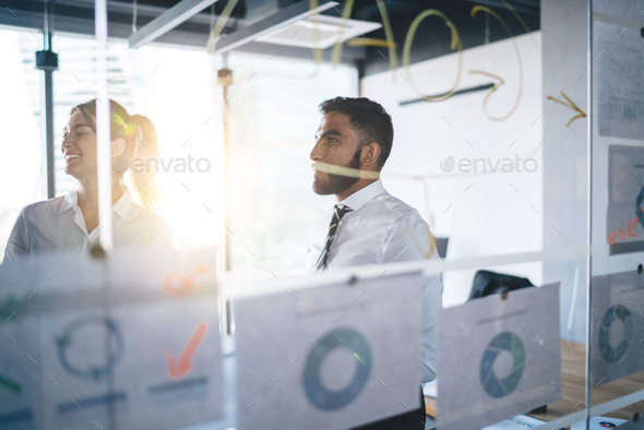 Cheerful male and female colleagues laughing near modern glass board ...